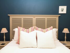 Uma cama com cabeceira, duas luminárias de apoio e um quadro na parede.