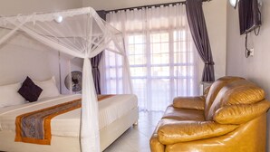 Quarto com cama, sofá de couro, ventilador ao lado da cama e janela com cortinas.