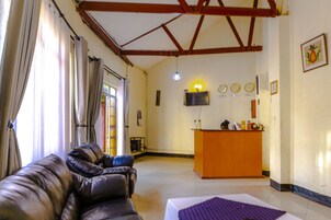 Uma sala de estar com sofá de couro, balcão de recepção de madeira e televisão fixada na parede.