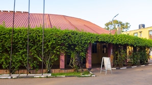 Um edifício com telhado vermelho, coberto por trepadeiras verdes, e uma área em frente com piso de tijolos.