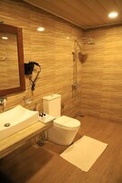 Uma casa de banho moderna com toucador de madeira, sanita, chuveiro e espelho.