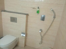 Casa de banho com sanita, chuveiro e dispensador de sabonete na parede.