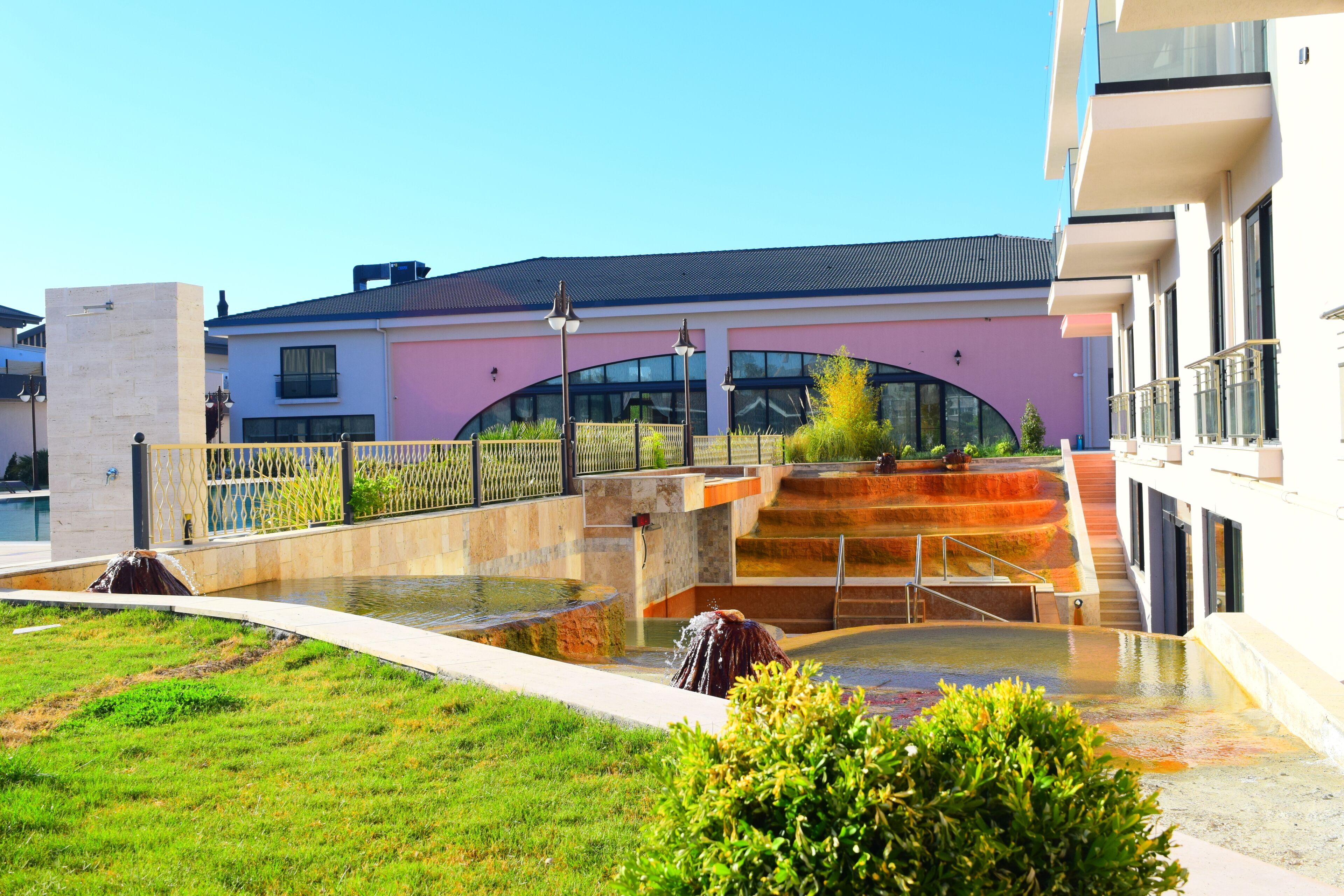 Um edifício moderno com fachada rosa, área de piscina com escadas e céu claro.