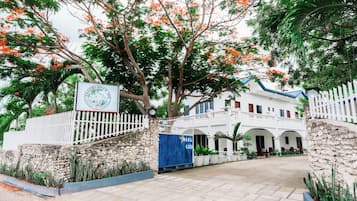 Entrada de hotel com parede de pedra, cerca branca e portão azul.