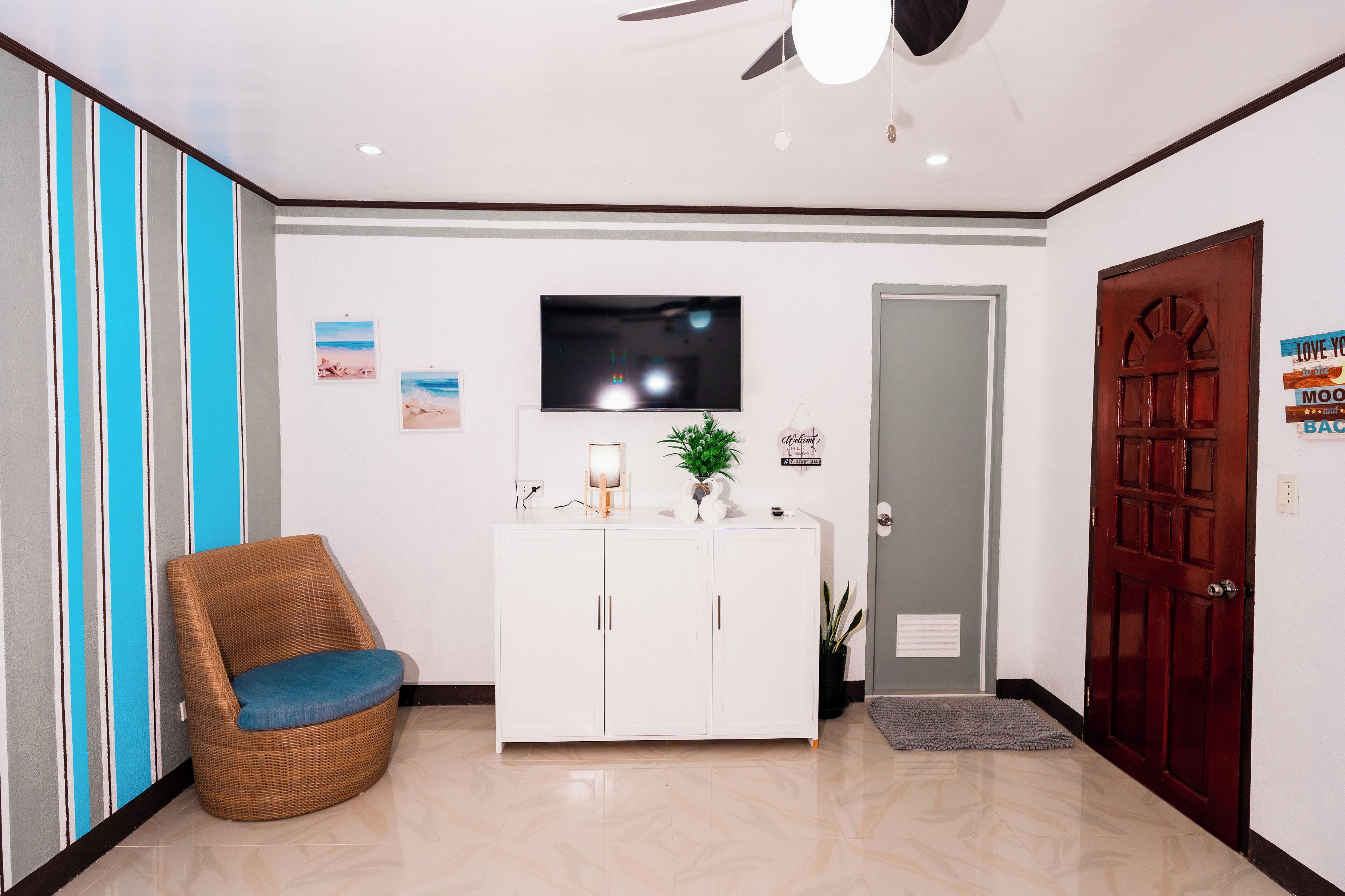 Uma área de recepção com uma cadeira de vime, um armário branco, uma televisão de tela plana e uma porta de madeira.