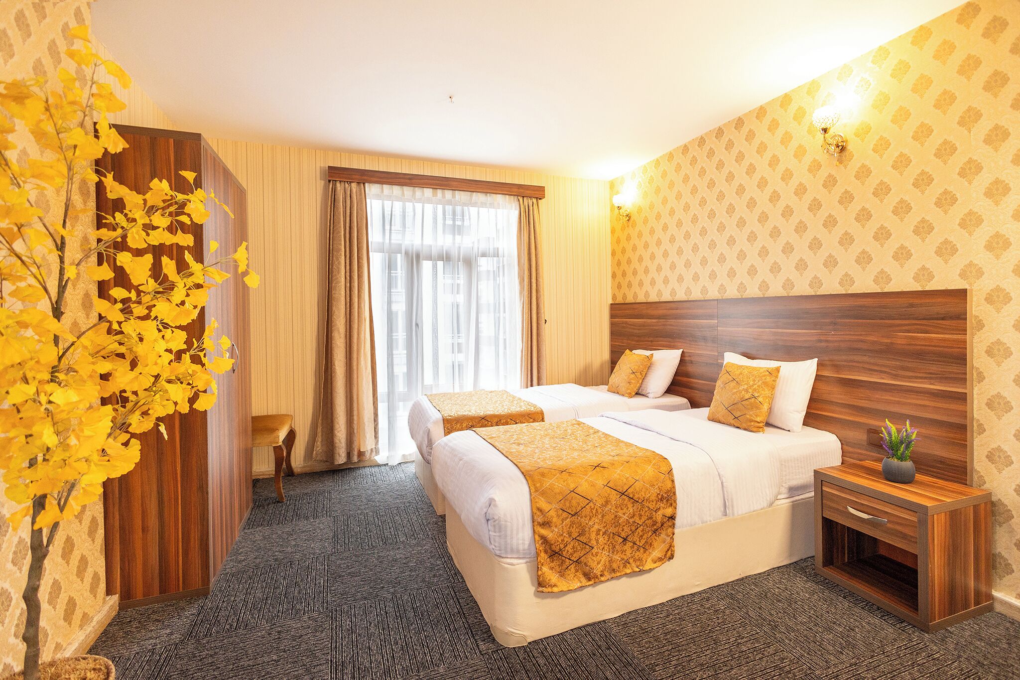 Quarto de hotel com duas camas, cabeceira de madeira, mesa de cabeceira e um vaso com planta.