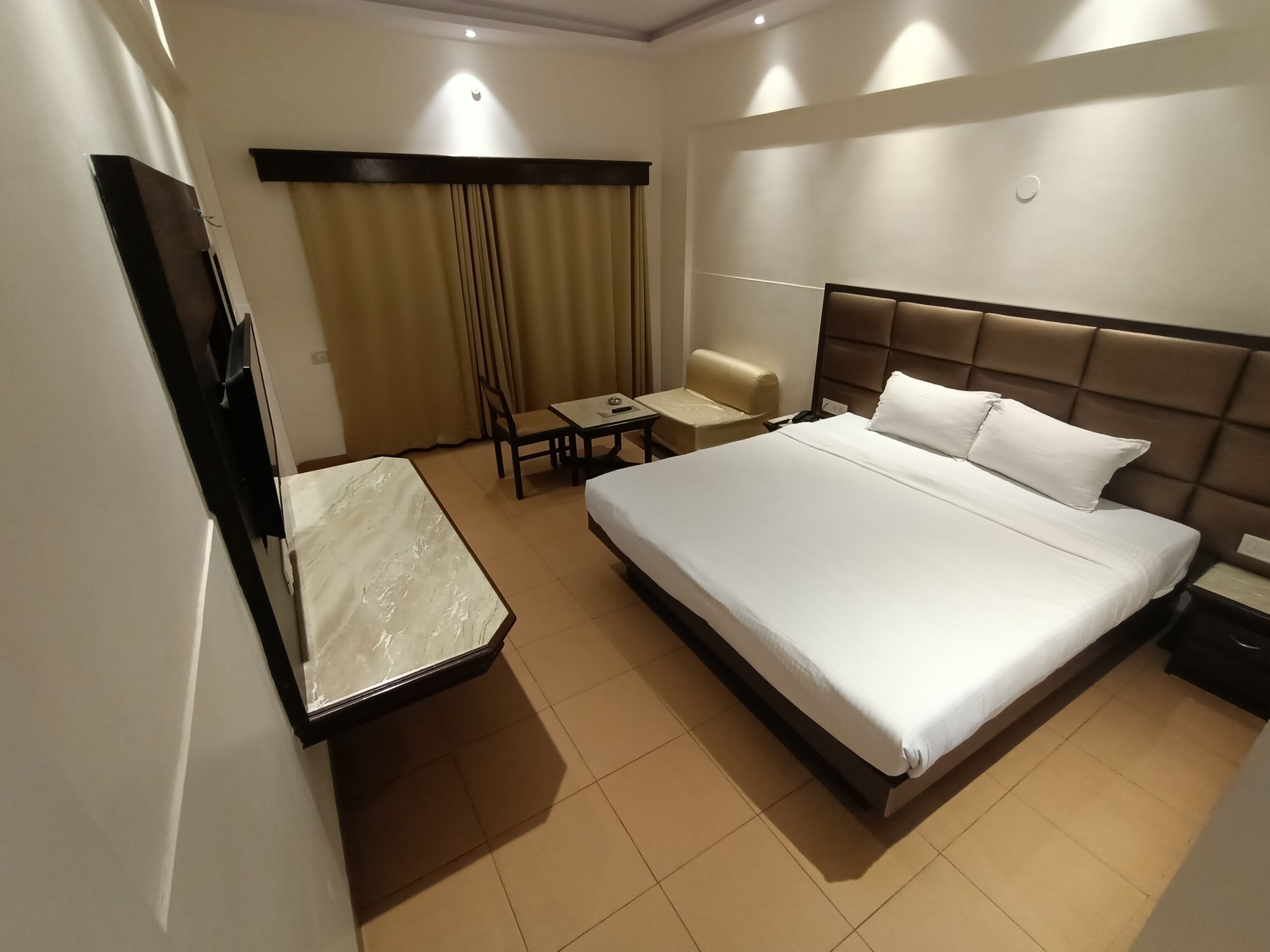 Quarto de hotel com uma cama grande, uma escrivaninha, uma cadeira e uma televisão.