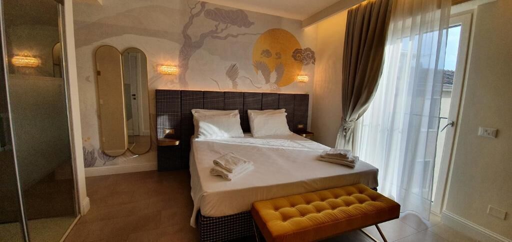 Um quarto moderno com uma cama grande, um banquinho, um espelho e uma parede com desenho decorativo.