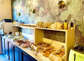Uma mesa de buffet com diversos alimentos, utensílios, uma torradeira e painéis decorativos na parede.