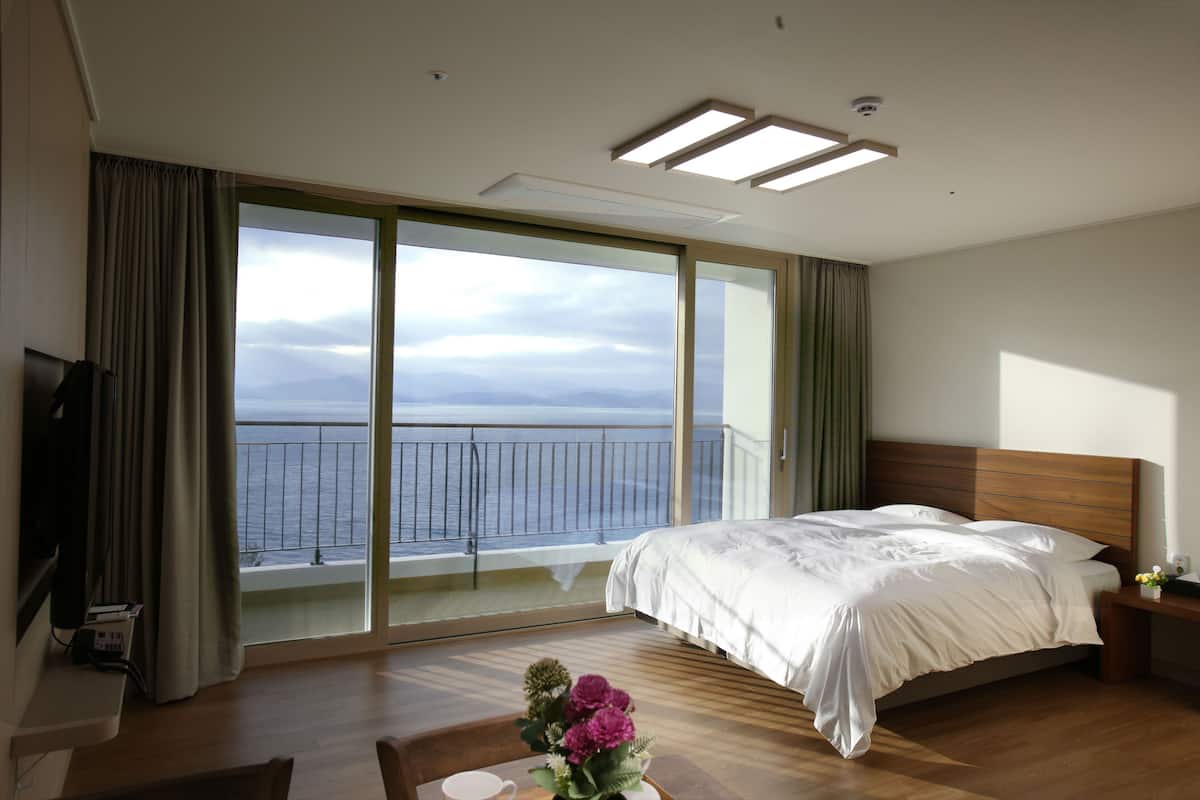 Quarto com uma grande porta de vidro deslizante que dá para uma varanda com vista para o mar.