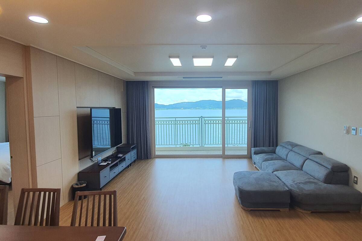Quarto de hotel com varanda, sofá, televisão e área de refeições.
