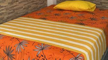 Quarto com cama, ar condicionado fixado na parede e colcha estampada.