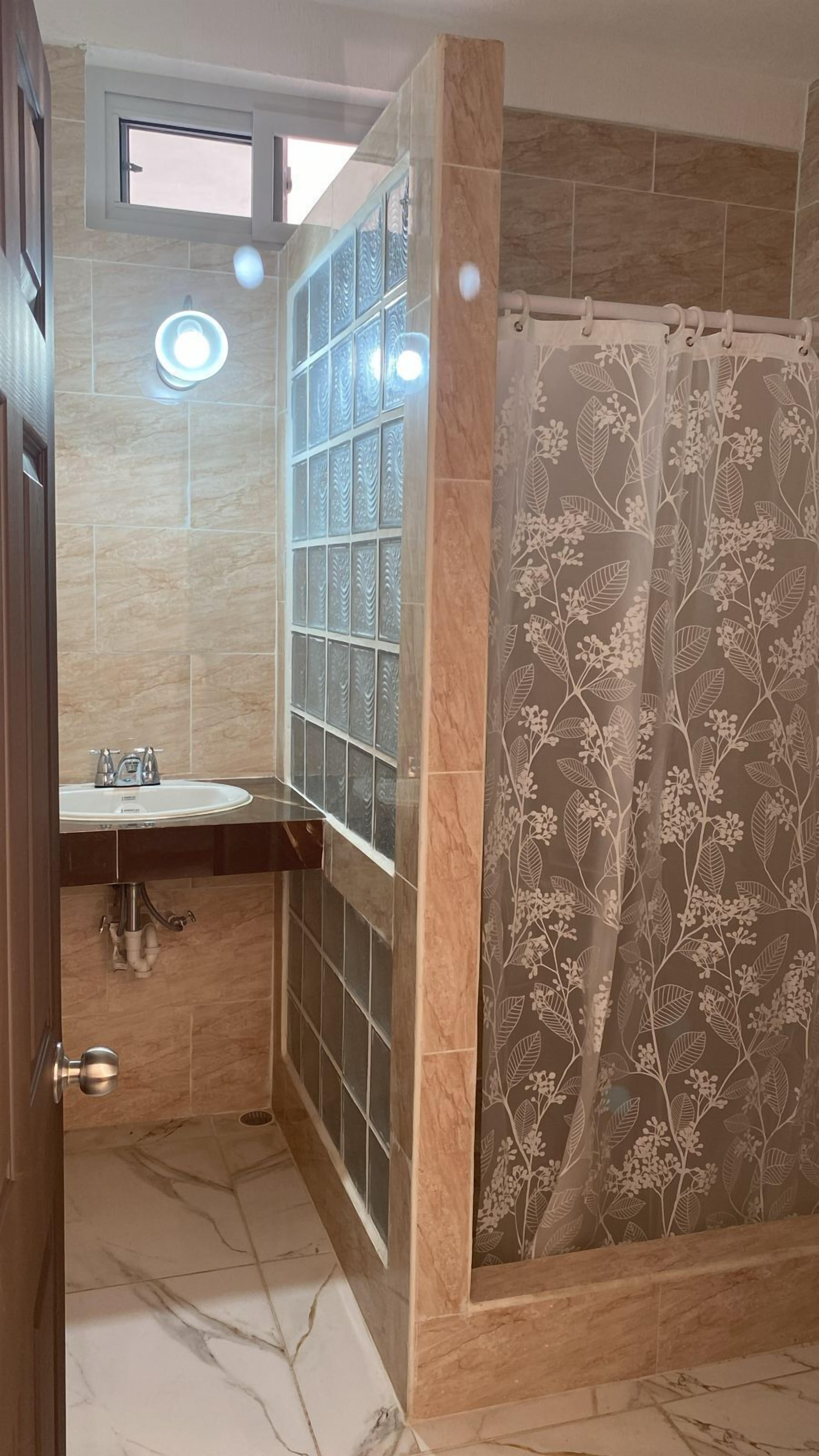Uma casa de banho com cabine de duche em vidro, lavatório com espelho e janela sobre o lavatório.