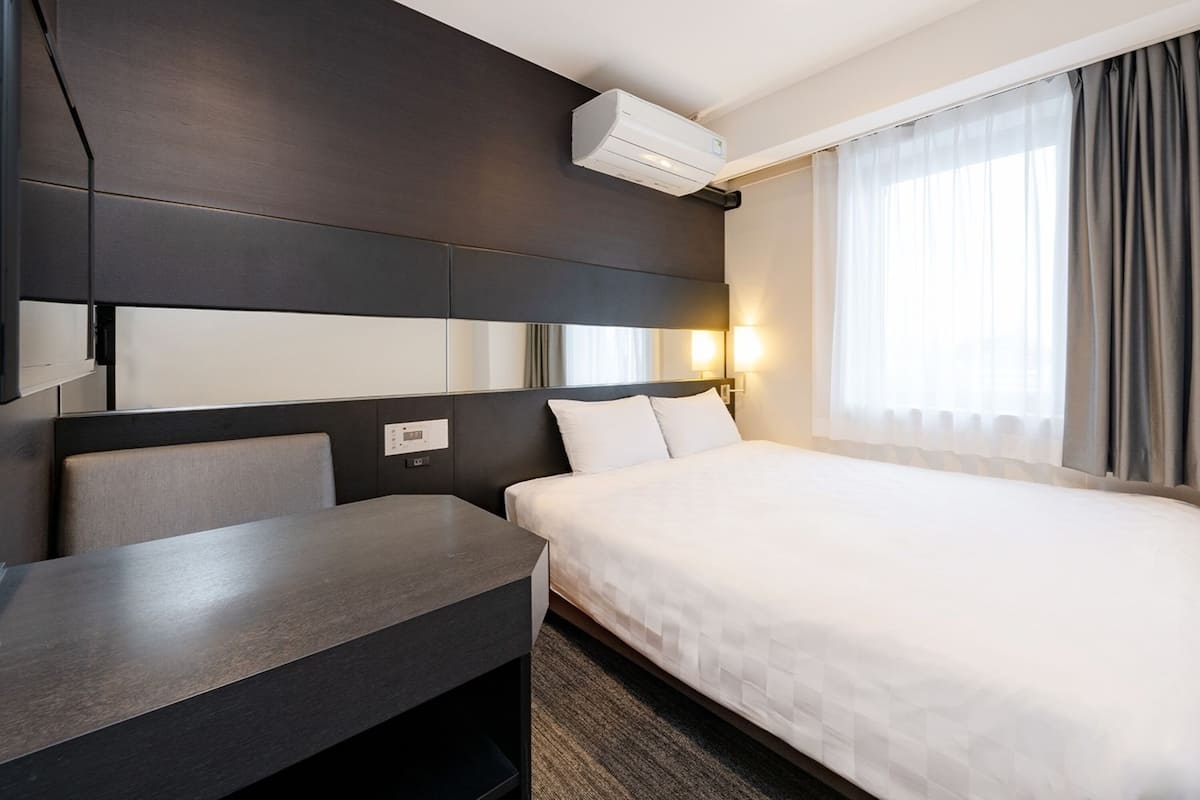 Quarto de hotel moderno com uma cama grande, uma escrivaninha e ar condicionado integrado.