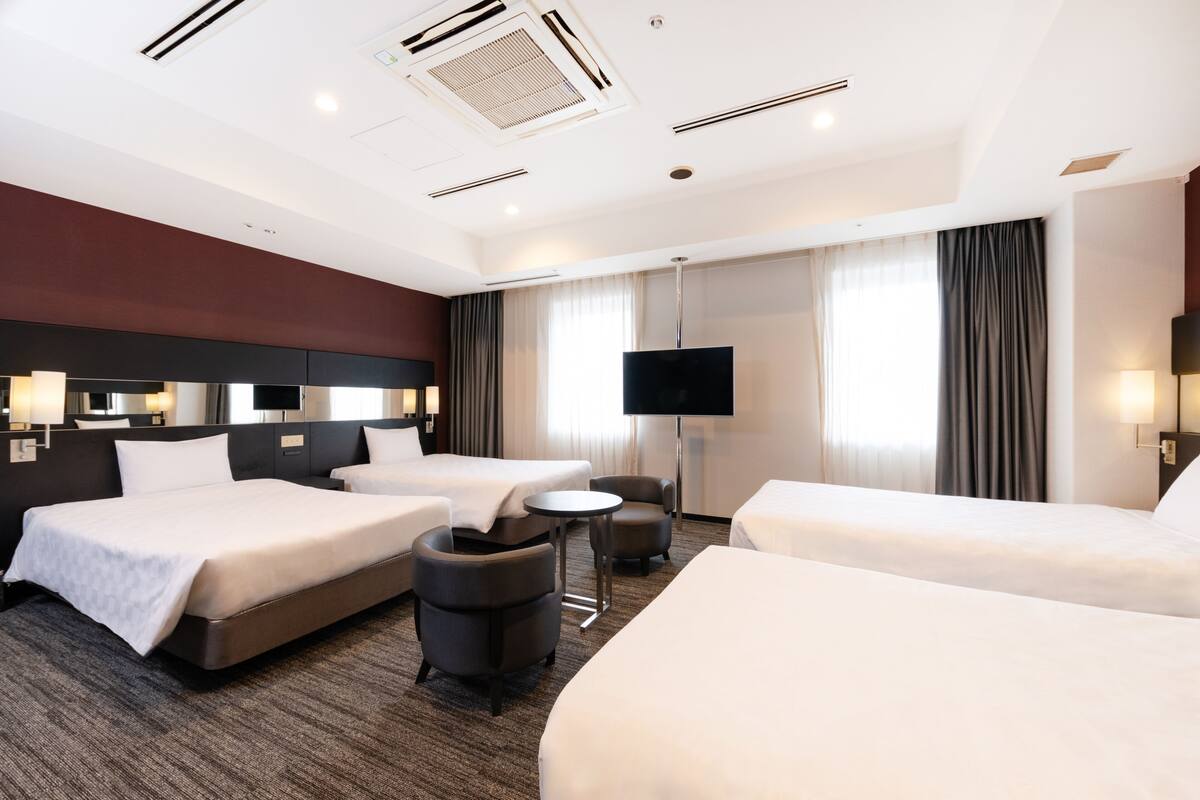 Quarto de hotel com duas camas, televisão de tela plana, uma mesinha e um sofá.