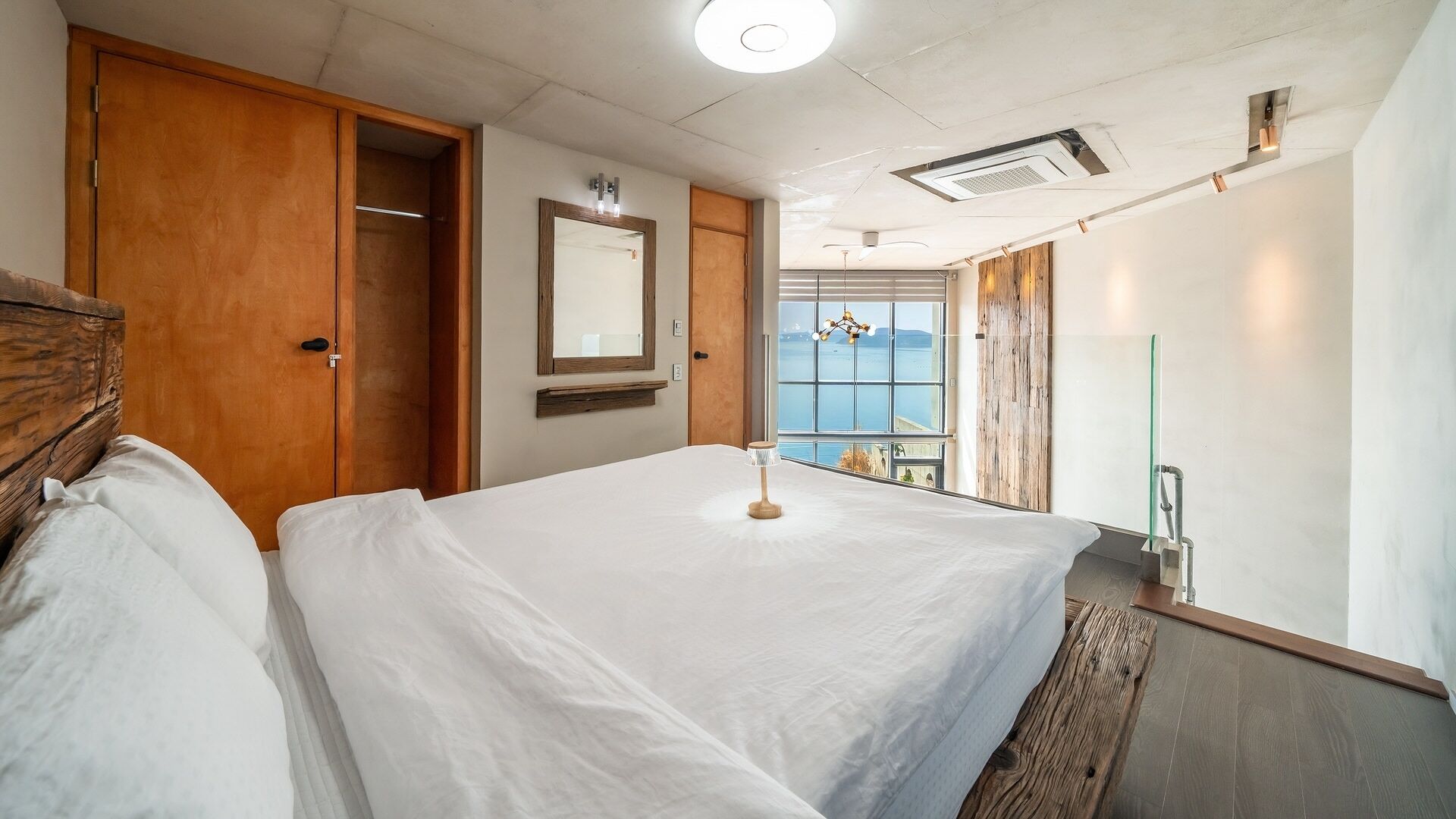 Quarto de hotel com uma cama grande, um guarda-roupa de madeira, um espelho e vista para o mar.