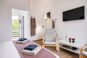 Quarto com cama, uma cadeira, televisão e janela com vista.