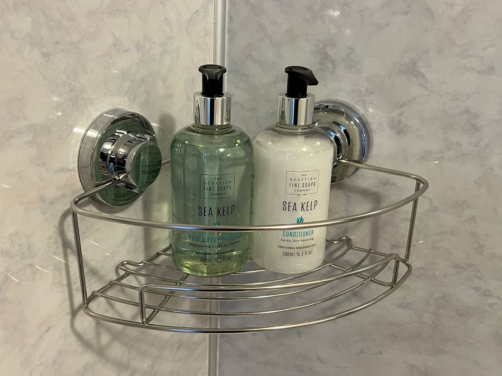 Um banheiro com uma prateleira de vidro que exibe duas embalagens de shampoo e condicionador para cabelo e corpo com extrato de alga marinha.