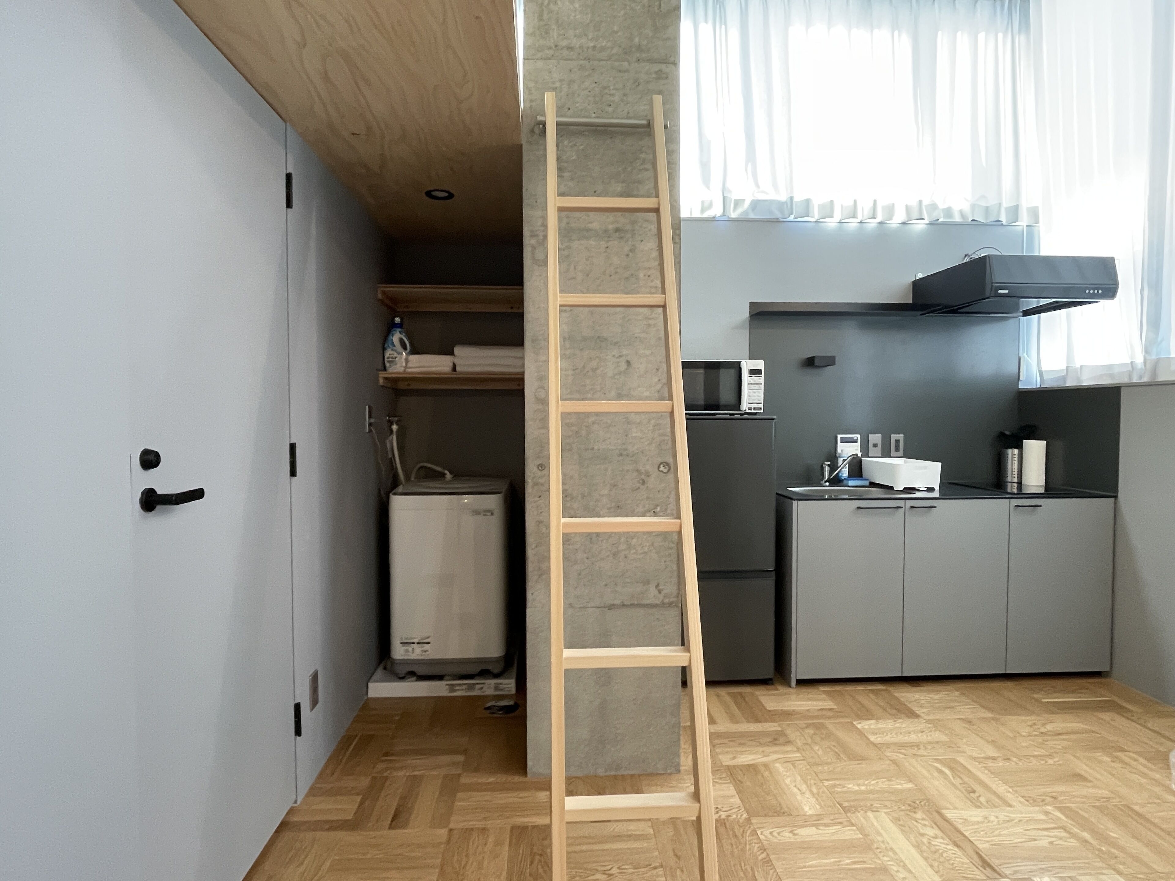 Uma cozinha compacta com micro-ondas integrado, geladeira e escada de madeira que dá acesso a um espaço de dormir no loft.