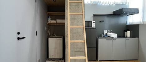 Uma cozinha compacta com micro-ondas integrado, geladeira e escada de madeira que dá acesso a um espaço de dormir no loft.