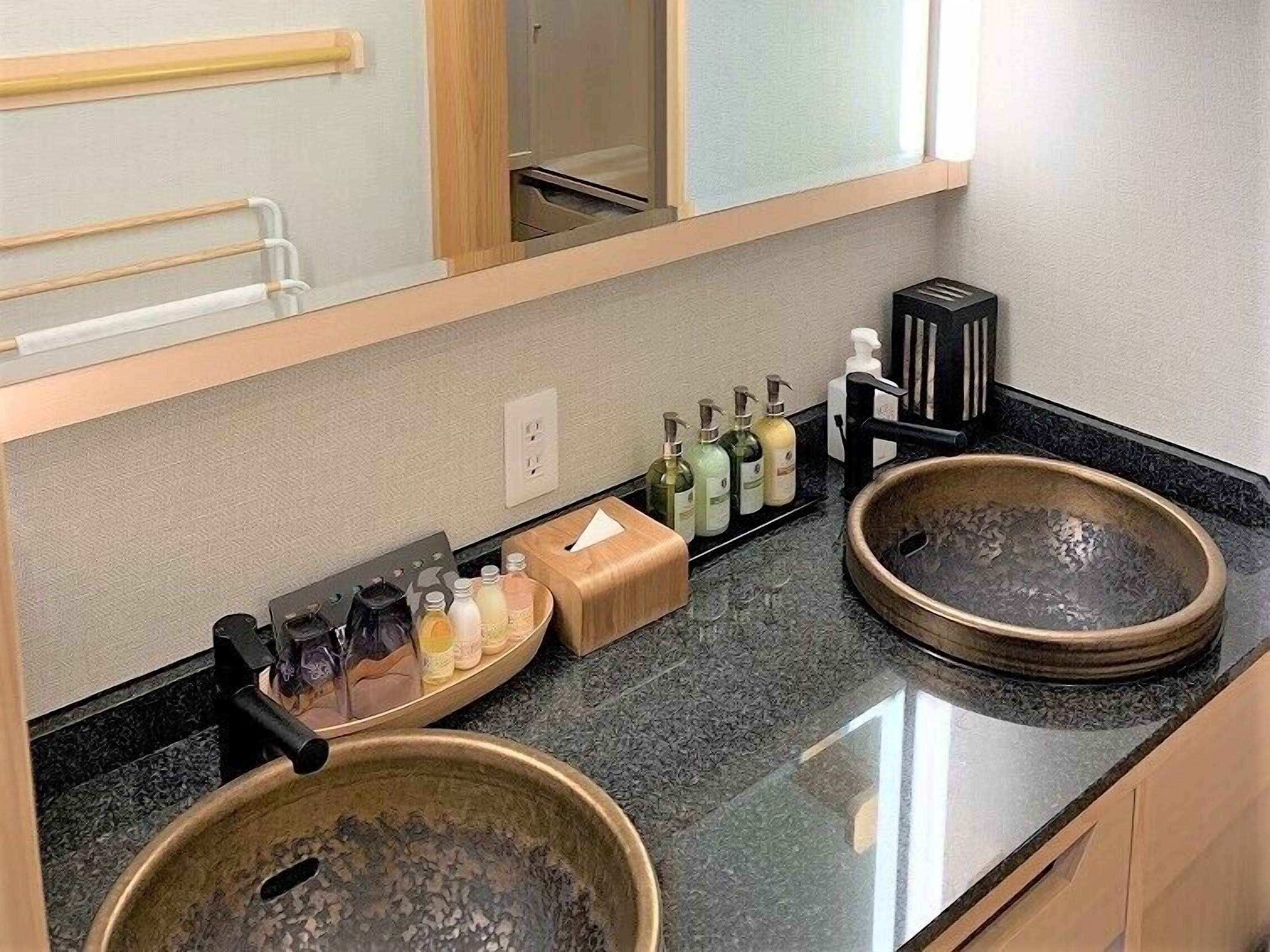 Casa de banho com duas pias, um espelho e um porta-toalhas. Há artigos de higiene pessoal sobre o balcão.