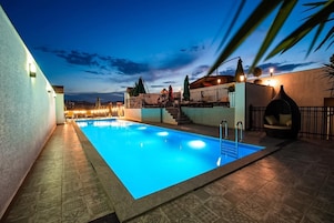 Piscina com superfície de água azul cristalina, rodeada por um deck revestido em azulejos e uma escadaria que leva a um nível superior.