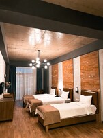 Quarto de hotel com duas camas, piso de madeira, parede de tijolos e teto com vigas aparentes.