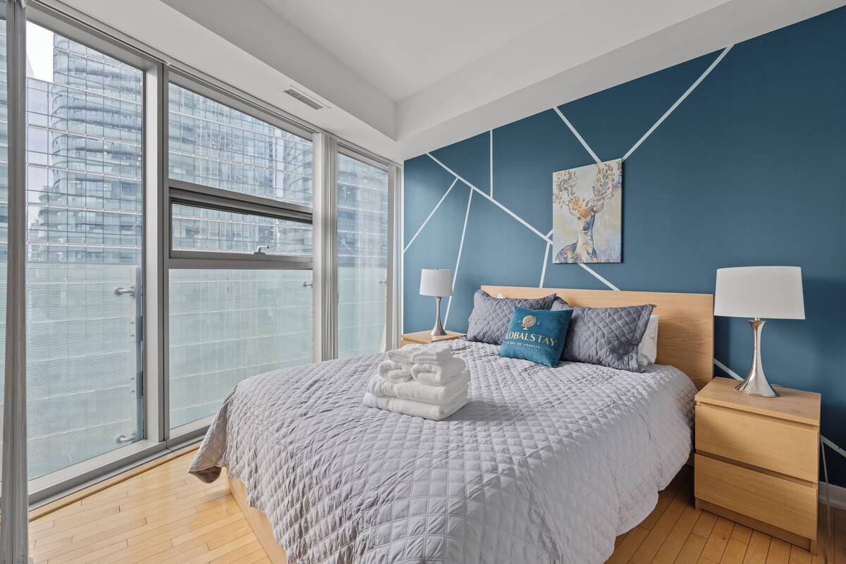 Quarto moderno com uma cama grande, duas mesas de cabeceira, uma janela e vista para a cidade.