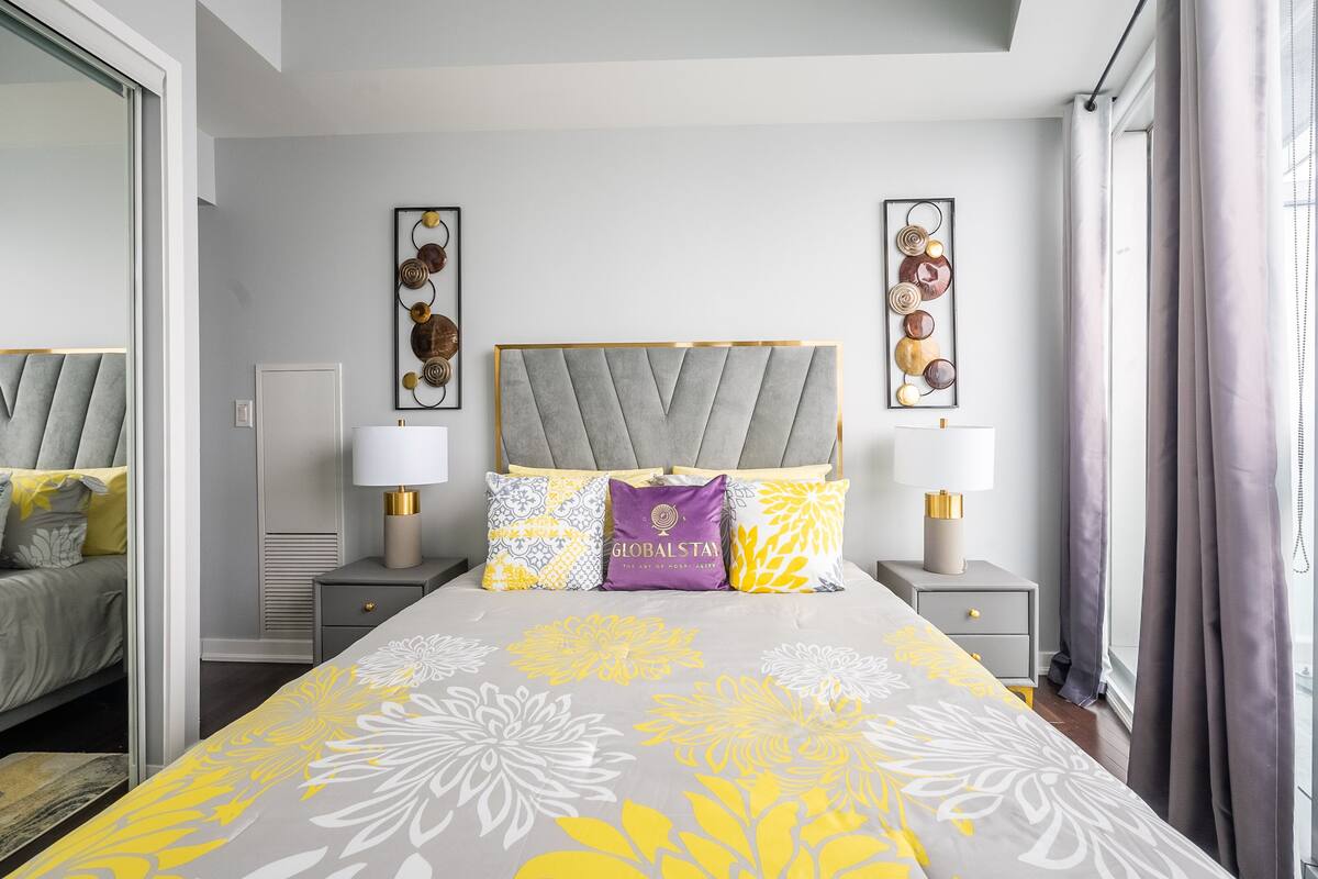 Quarto de hotel moderno com uma cama grande, duas mesas de cabeceira, cabeceira e arte decorativa na parede.