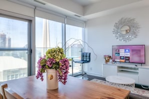 Uma sala de estar moderna com uma mesa de madeira, uma planta em vaso, uma cadeira azul, uma TV e um espelho decorativo.