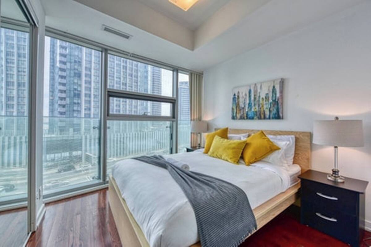 Quarto de hotel moderno com uma cama grande, mesa de cabeceira, luminária e um quadro na parede.