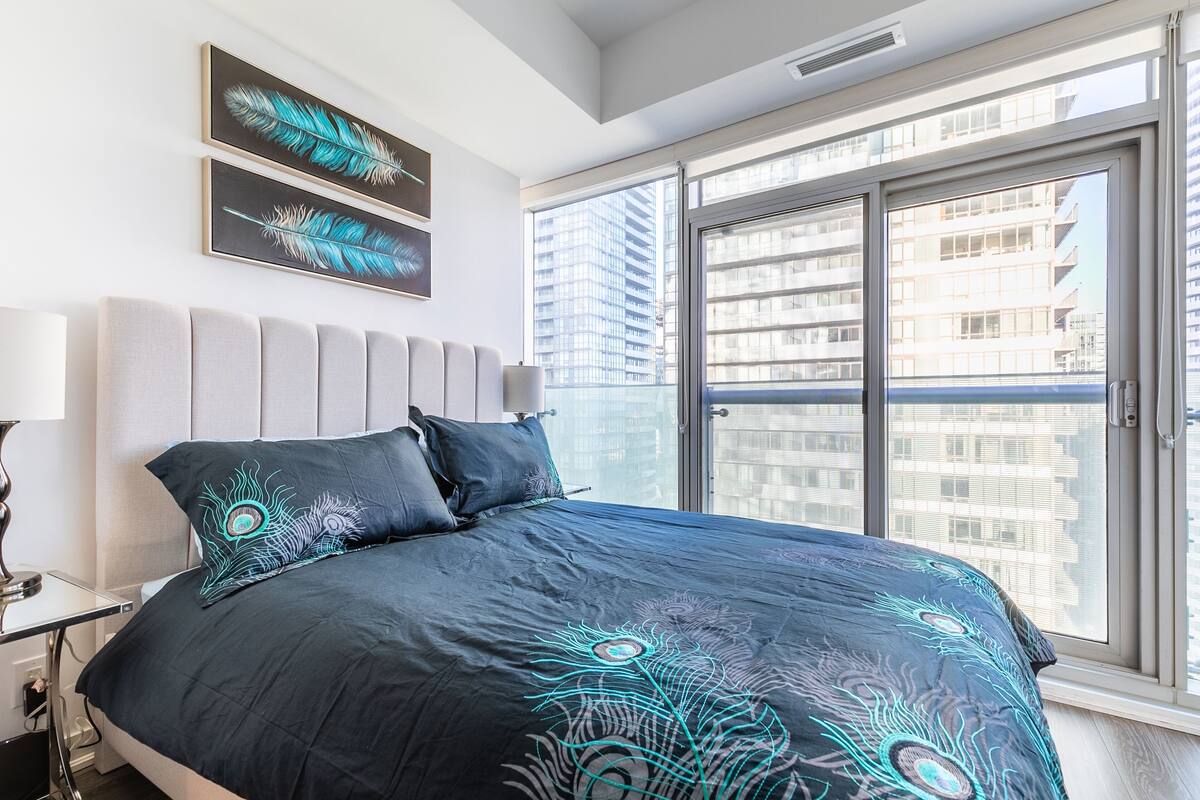 Quarto moderno com uma cama grande, vista da cidade através de uma porta deslizante e obras de arte na parede.