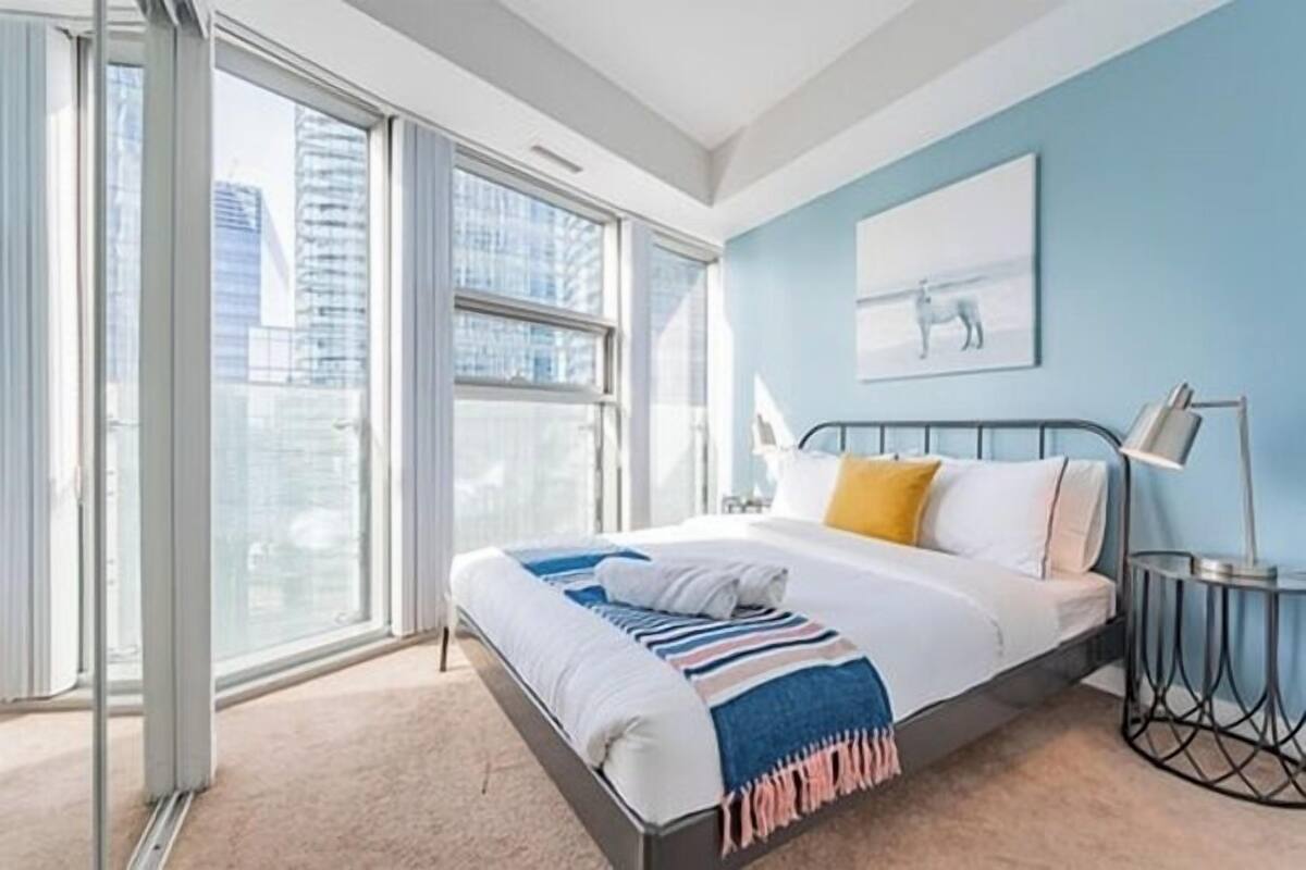 Quarto de hotel moderno com uma cama grande, vista para a cidade e uma obra de arte emoldurada na parede.