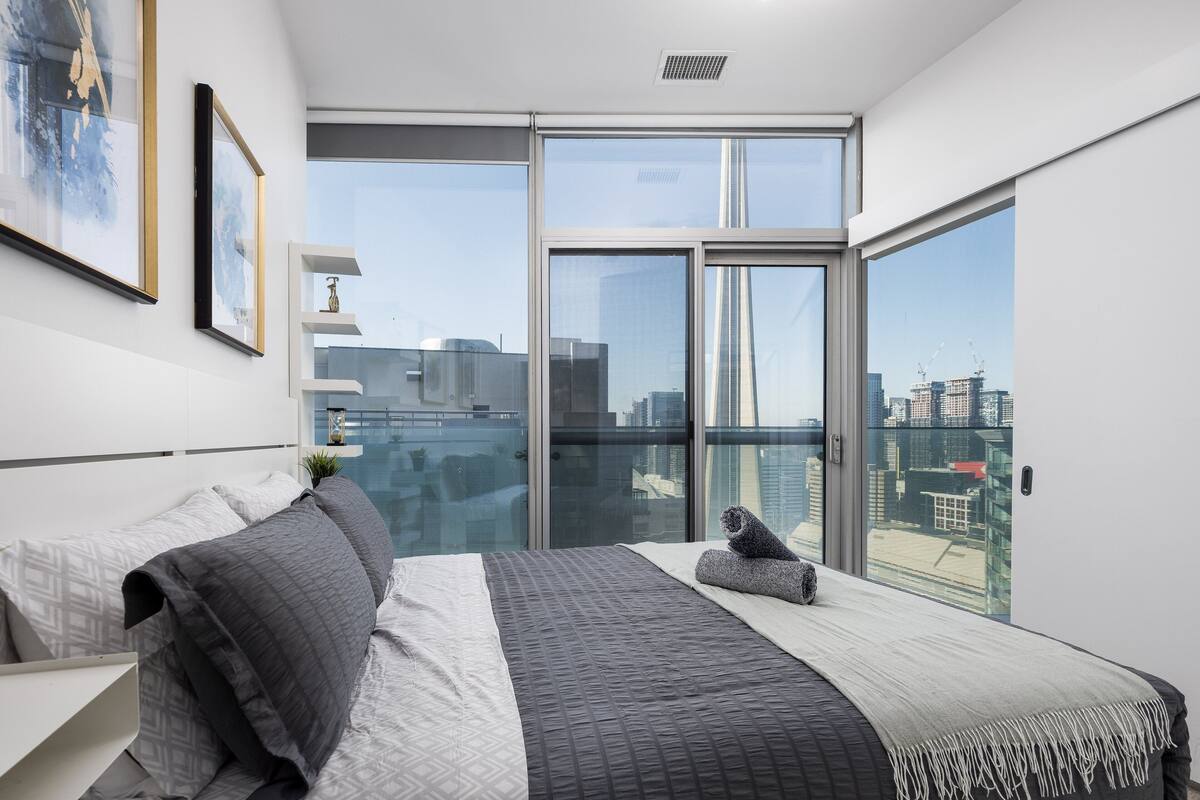 Quarto moderno com cama grande, vista para a cidade através de janelas do chão ao teto e design minimalista.