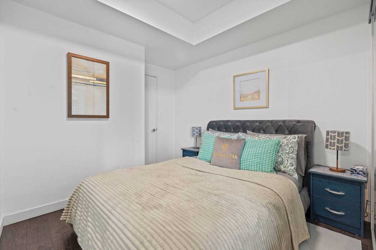 Quarto com cama, mesa de cabeceira, abajur e duas fotos emolduradas na parede.