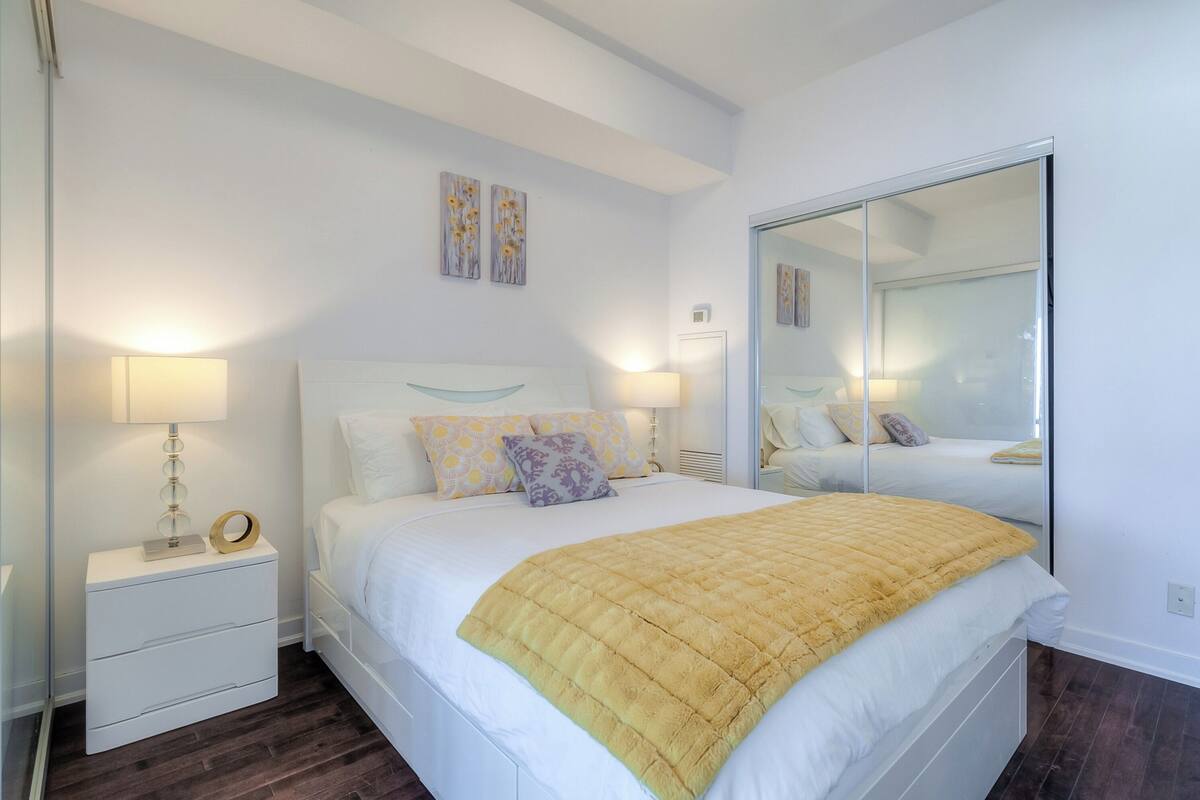 Quarto com cama, mesas de cabeceira, espelho e obras de arte na parede.