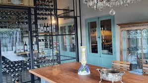 Uma sala de jantar com mesa de madeira, cadeiras, um candelabro e um aparador com garrafas de vinho.