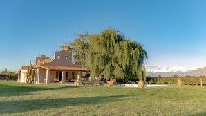 Uma casa com um pátio, uma árvore grande e uma montanha ao fundo.
