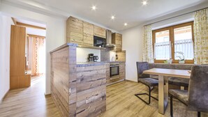 Cozinha moderna com armários de madeira, área de refeições com mesa e cadeiras, e janela com cortinas.