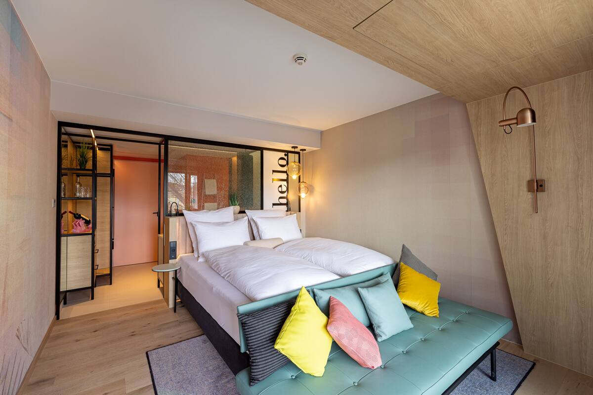 Quarto moderno com cama, um banquinho e um guarda-roupa.
