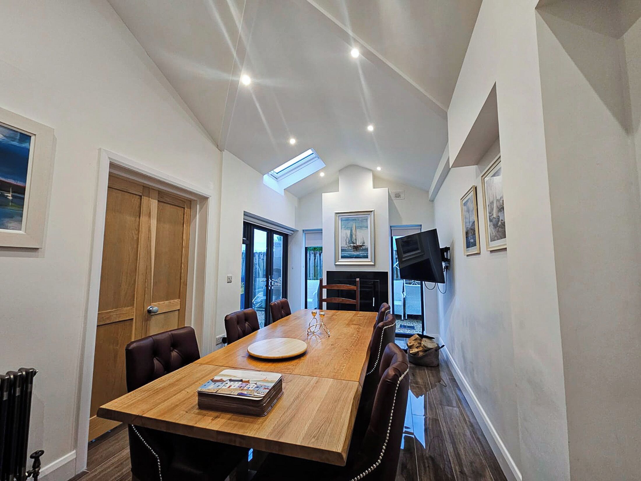 Uma sala de jantar moderna com uma mesa de madeira, cadeiras de couro e uma televisão.