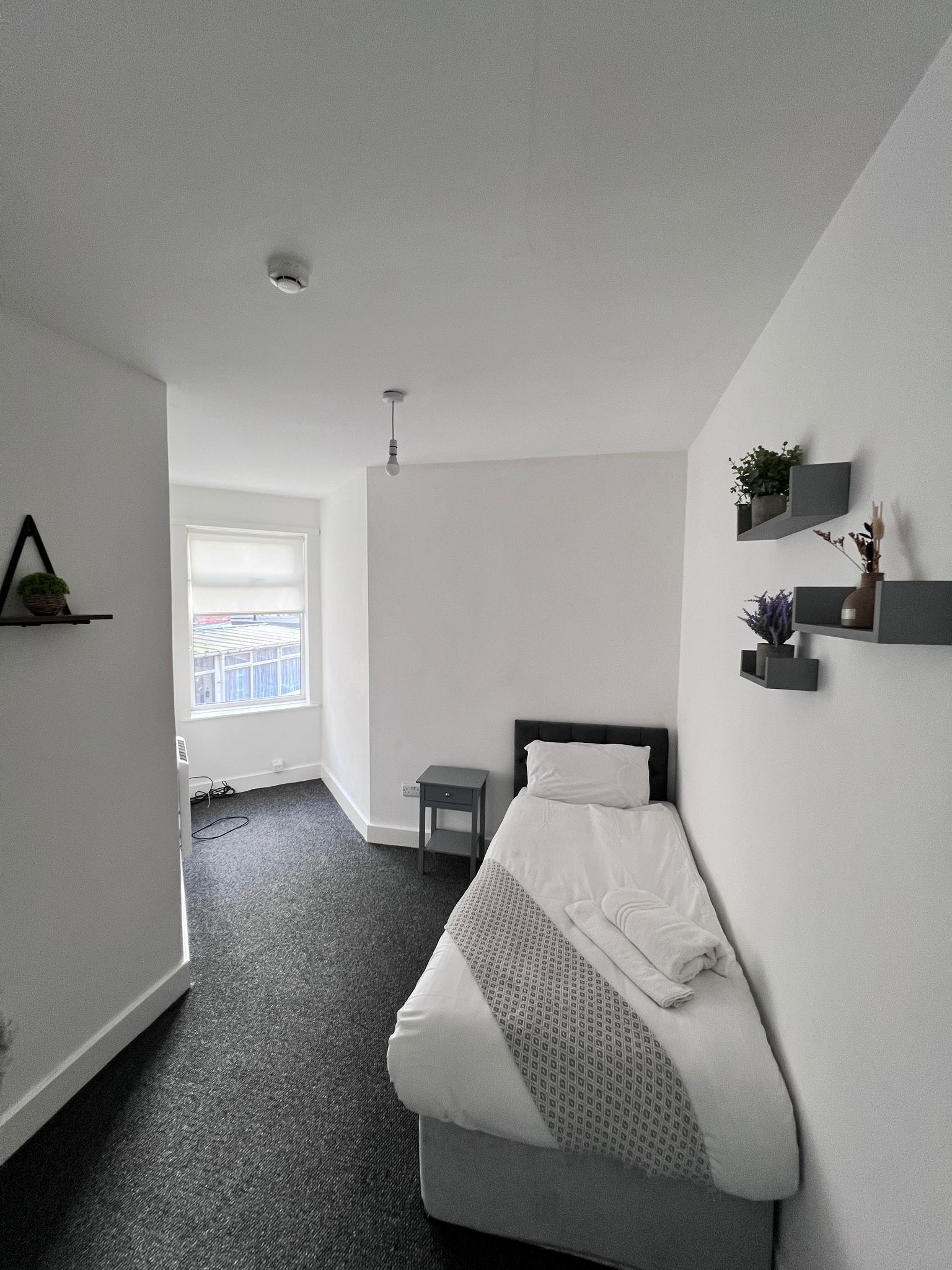 Quarto de hotel moderno com cama, mesa de cabeceira e uma pequena janela.