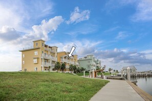 Um edifício residencial com vários andares, uma área gramada na frente e um cais que se estende sobre a água.