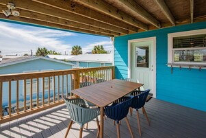 Um deck de madeira com uma mesa e cadeiras, uma parede azul e uma porta com janela.