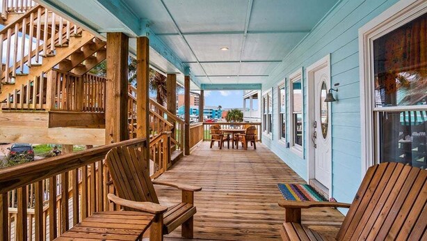 Um deck de madeira com cadeiras, uma mesa e uma escadaria, com vista para o oceano.