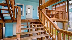 Escada de madeira que dá acesso a um segundo andar, com uma parede externa azul e uma porta branca com vitral decorativo.