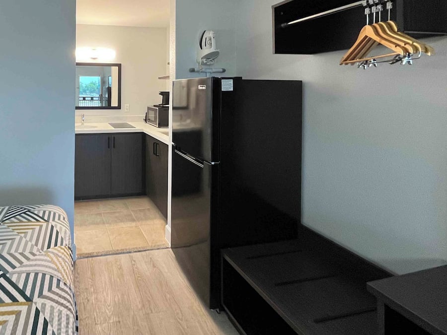 Quarto compacto com cama, pequeno espaço de cozinha, frigorífico e um cabideiro.