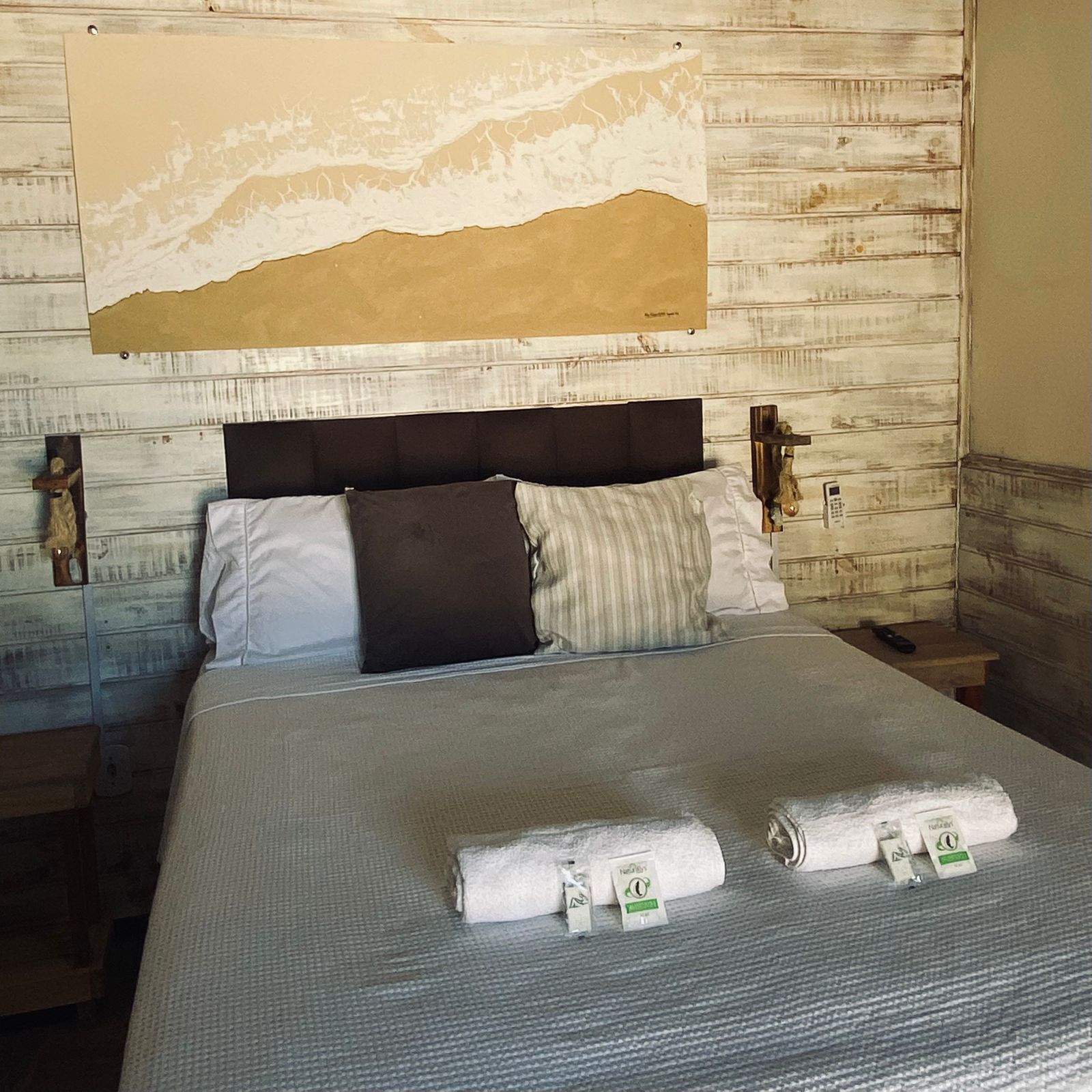 Cama com almofadas, cabeceira e uma obra de arte na parede.