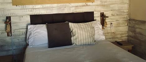 Cama com almofadas, cabeceira e uma obra de arte na parede.