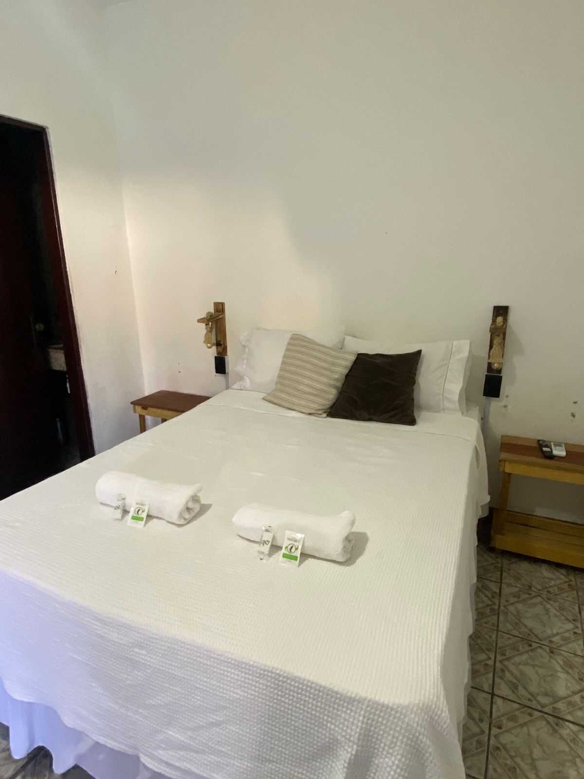 Quarto de hotel com cama bem arrumada, mesa de cabeceira e criado-mudo.